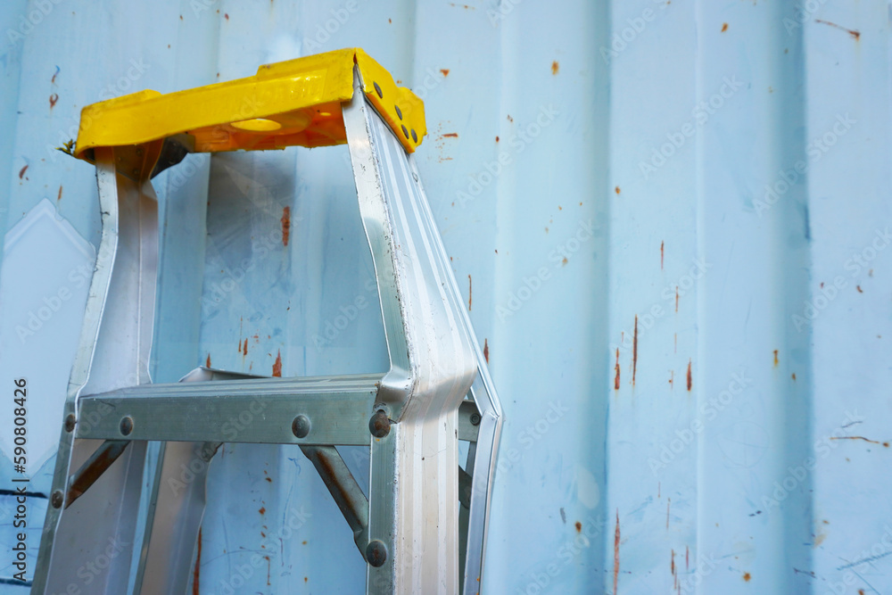 Aluminum folding ladder damaged (A-Type) is leaning against a container ...
