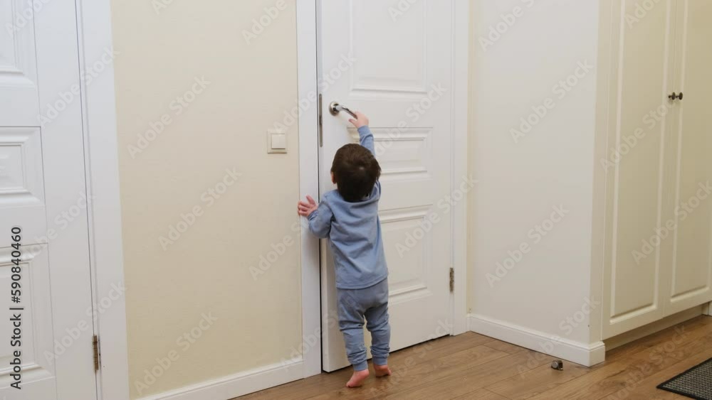 Little baby opens the door. Child pulls the door handle with the lock ...