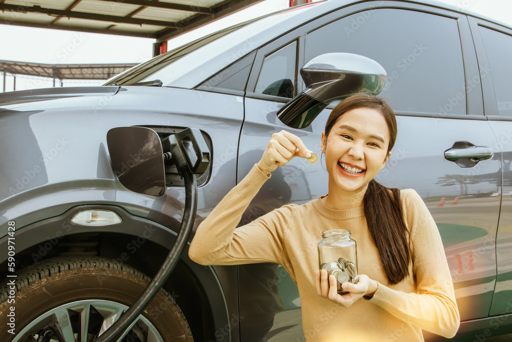 Portrait young asian woman driving an EV electric vehicle during charging, smiling good mood ...