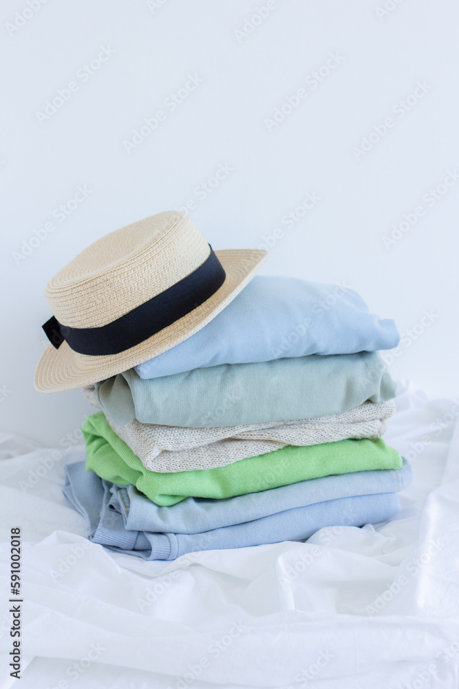 Foto de Pile of clothes with straw hat on white, pastel color palette ...