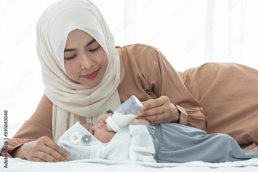 Happy Asian young Muslim mother wear hijab holding milk bottle, feeding ...