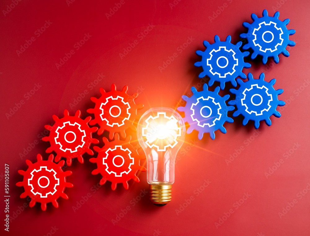 Glowing light bulb connected between blue and red gear wheels on red ...