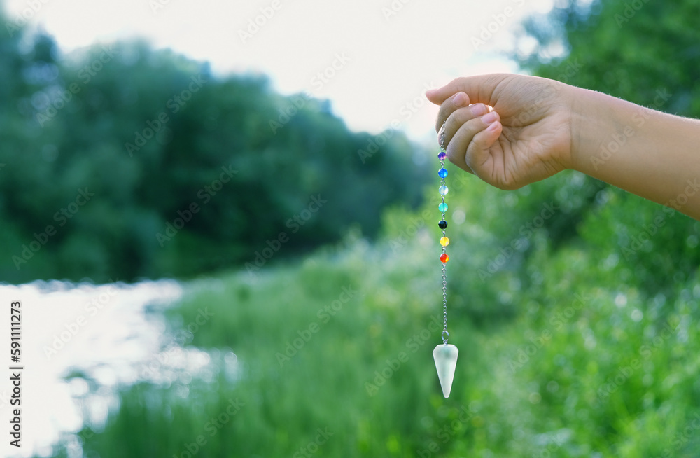 Hand holding dowsing pendant against abstract green natural background ...