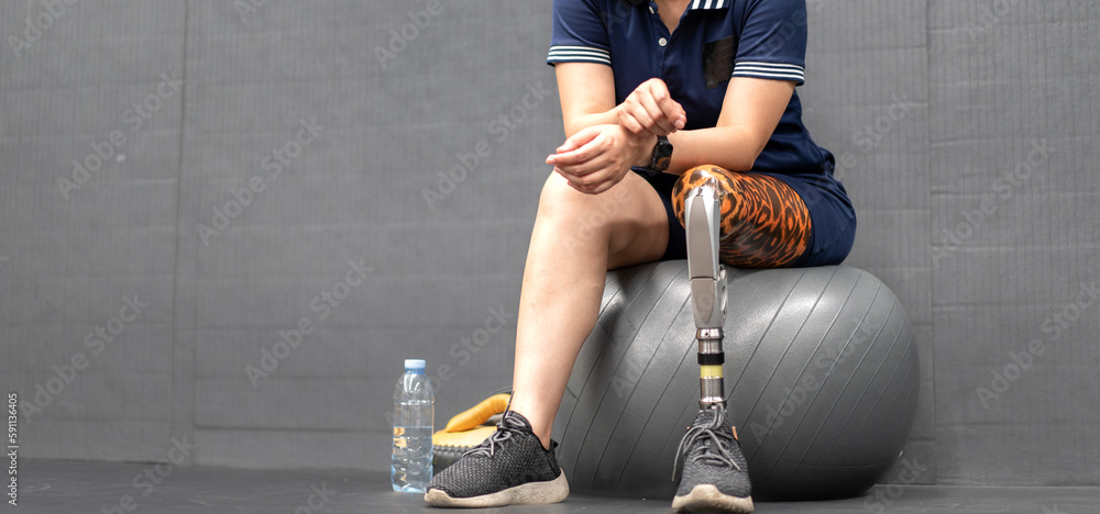 Asian woman with prosthetic leg sits isolated in gym. Young girl with ...