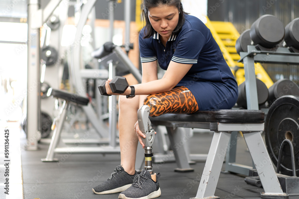 Asian woman with prosthetic leg lifting weight in gym. Young girl with ...