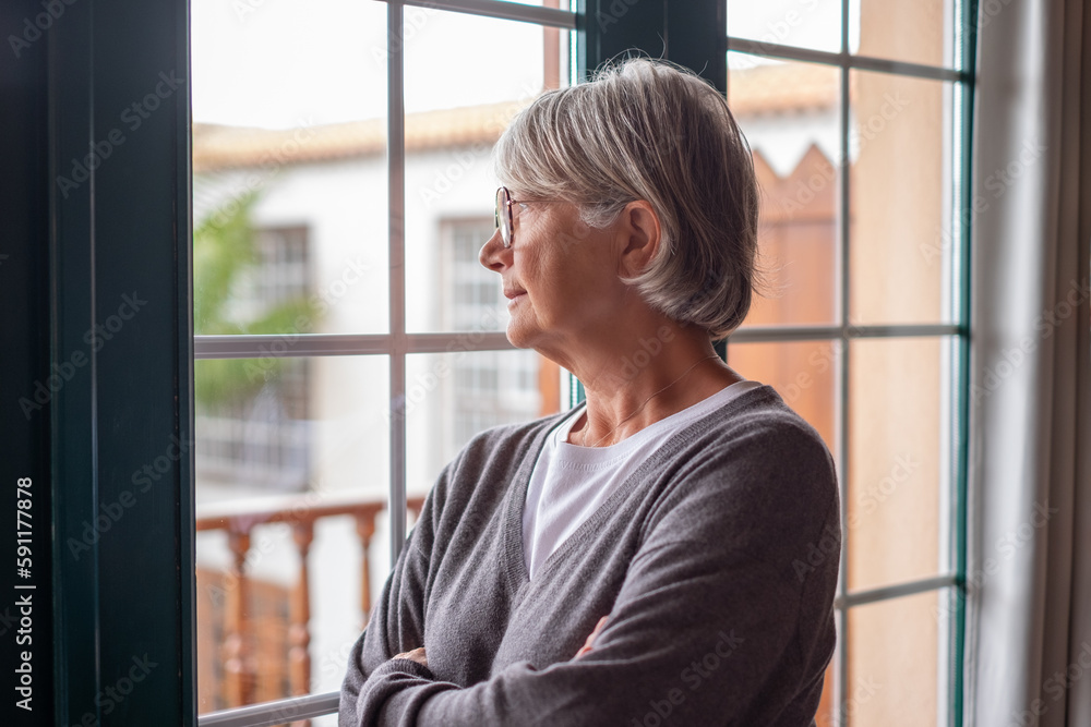 Old senior woman standing at window looking outside. Thoughtful old ...