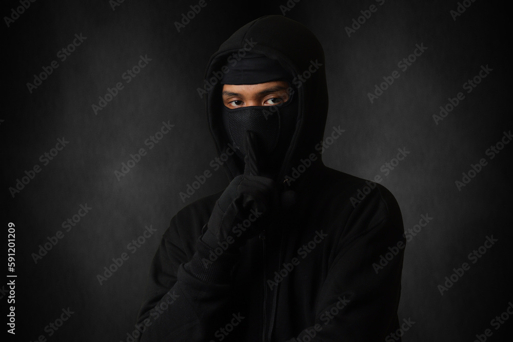 Mysterious man wearing black hoodie and mask standing against dark ...