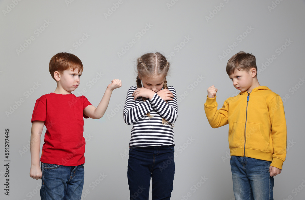 Boys with clenched fists looking at girl on light grey background ...