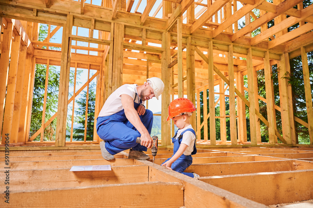 Father with toddler son building wooden frame house. Builder teaching ...