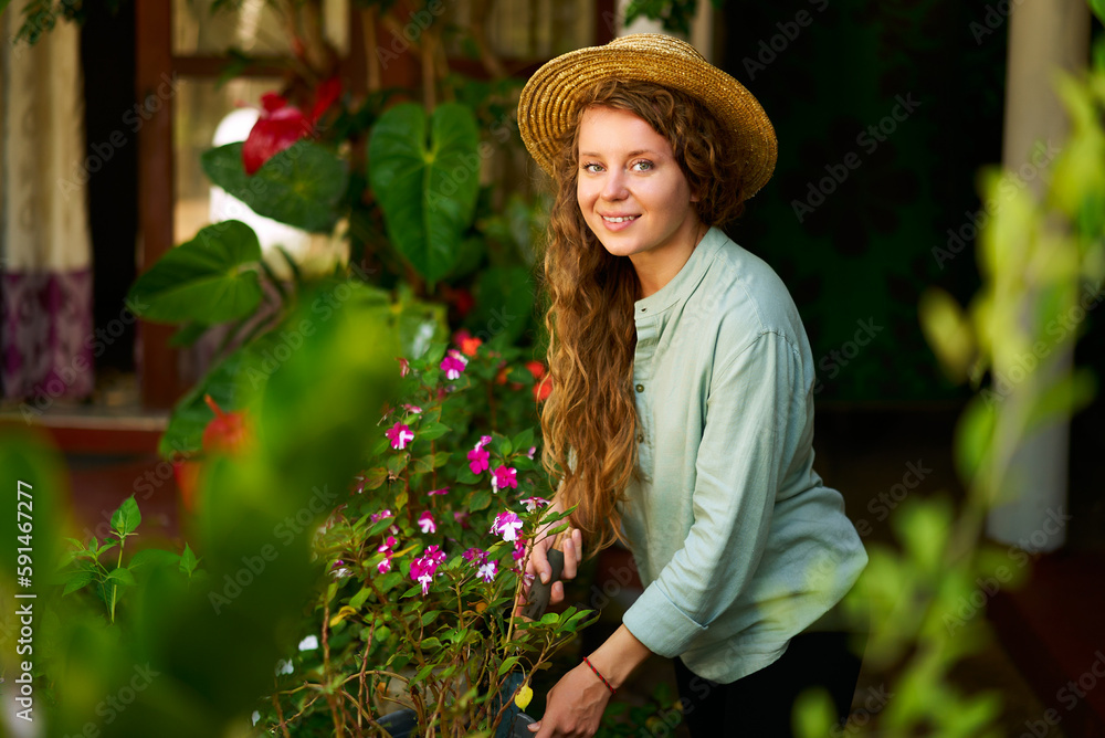 Young woman stands in garden planting flowers in pots smiles and looks ...