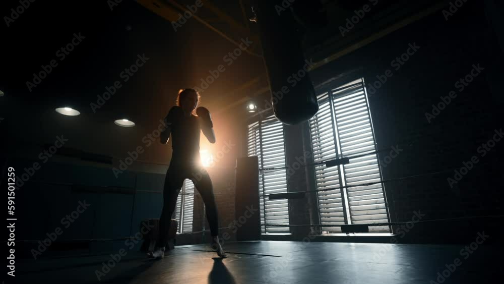 Woman boxer practicing punches using punching bag in gym on boxing ring ...