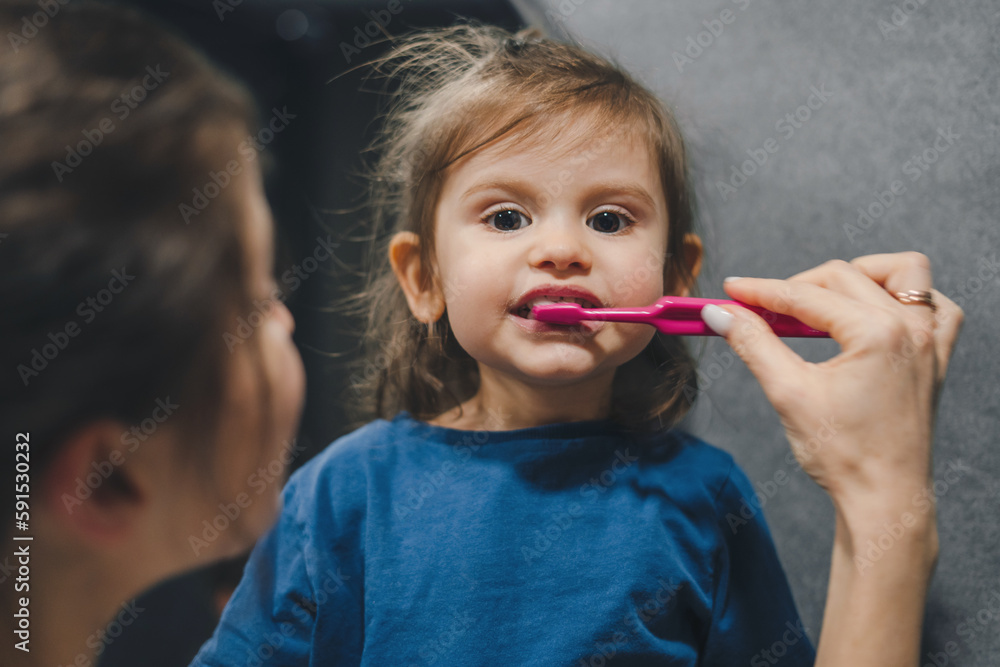 Back view of a mother helping out a little adorable girl brushing teeth ...