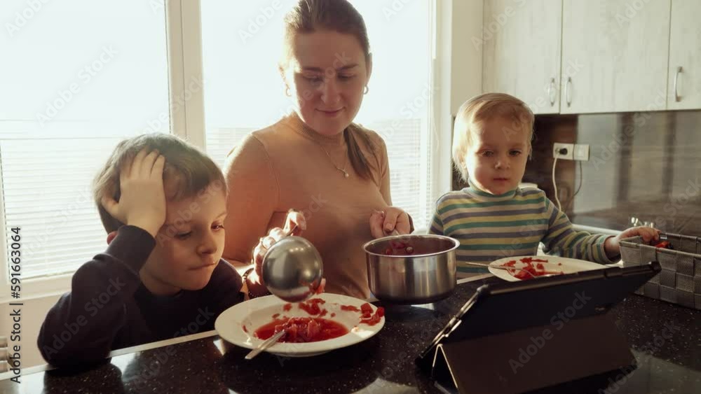 Two little boys watching video on tablet computer while mother is ...