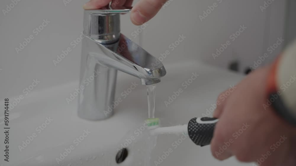 Closed shot of male arm holding a power toothbrush under tap in ...