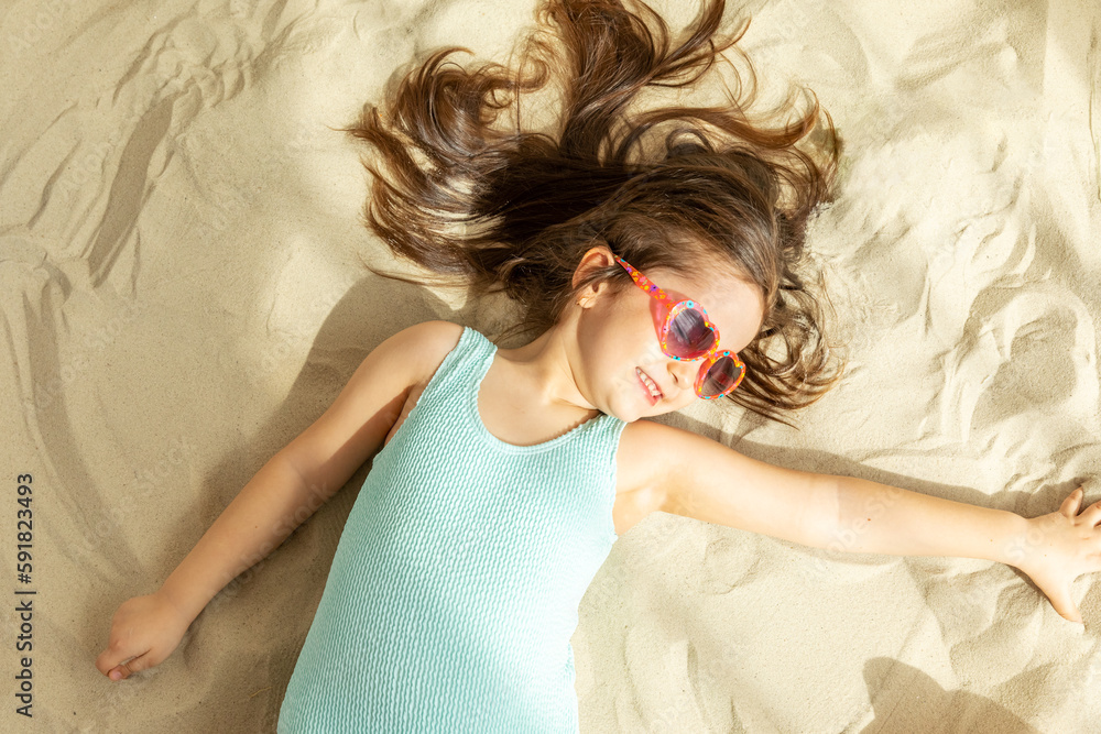 Happy cute little girl lying on a sandy beach and sunbathe in the sun ...