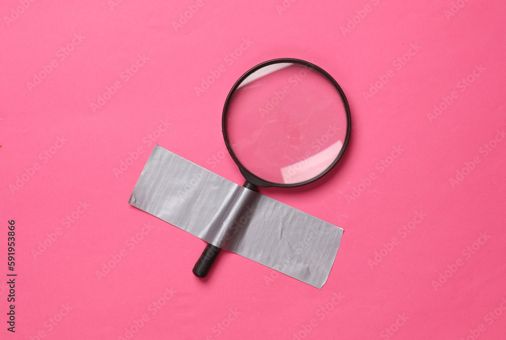 Magnifying glass fixed with adhesive tape on a pink background ...