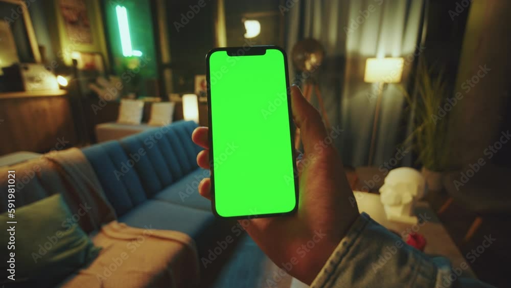 Hand man holds a scrolling phone with a vertical green screen in a dark ...