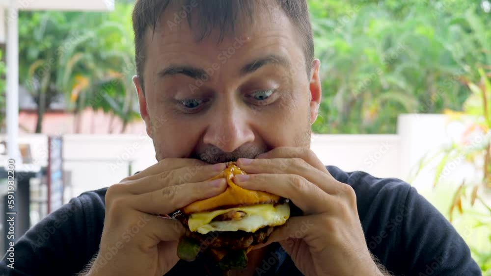 Man eat juicy hamburger at an outdoor restaurant. Man enjoys delicious ...