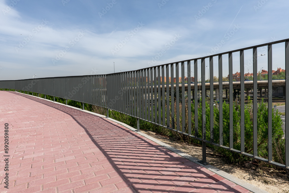 Brick pathway with metal railing casting shadow over them in an urban ...