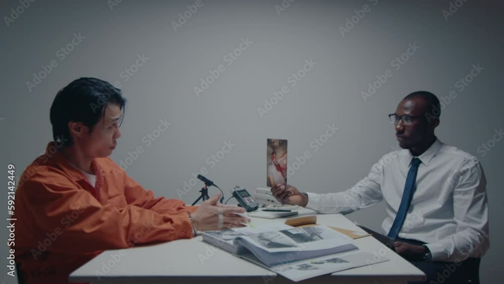 Black male detective showing crime scene photos to arrested murderer ...
