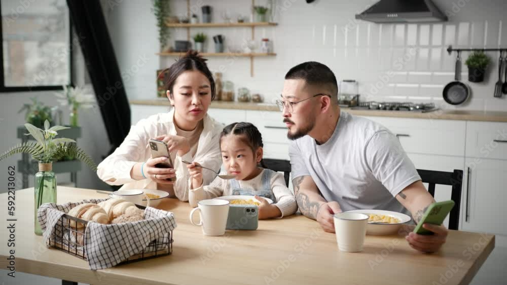 Family Eating Using Gadgets. Asian family eats corn flakes and watches ...