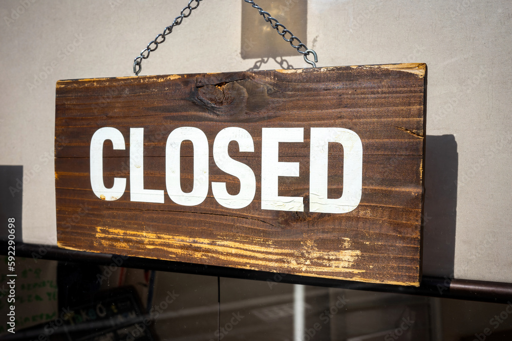 Brown wooden sign hanging in front of a closed door with the words ...