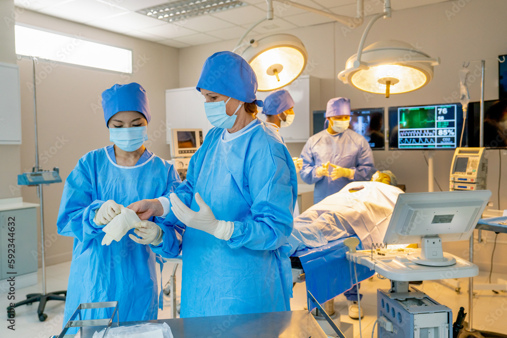 Professional nurse help the doctor to wear surgical gloves before ...