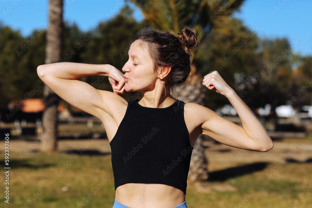 Young beautiful woman in sportswear raises arms to show muscles, biceps ...