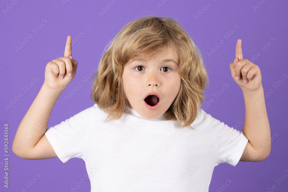 Surprised child pointing up finger on isolated studio background ...