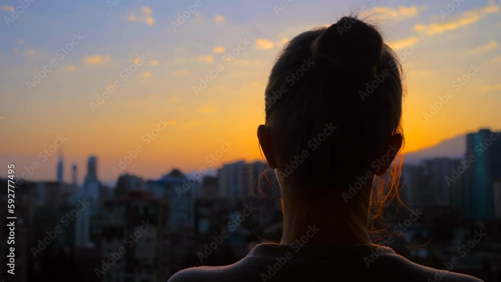Back view: woman silhouette is standing on the balcony and looking at ...