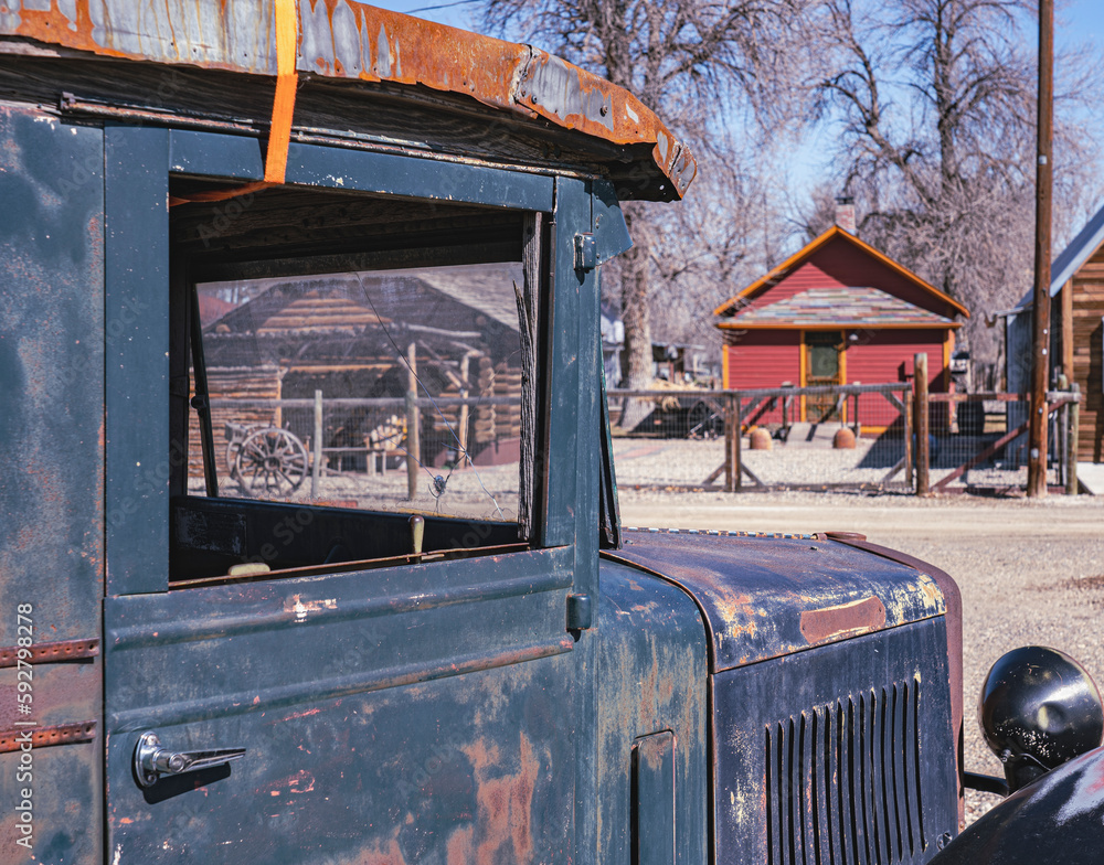 Jalopy old antique truck car faces a street of log houses & buildings ...