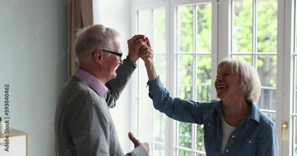 Cheerful energetic mature couple dancing to music together at home ...