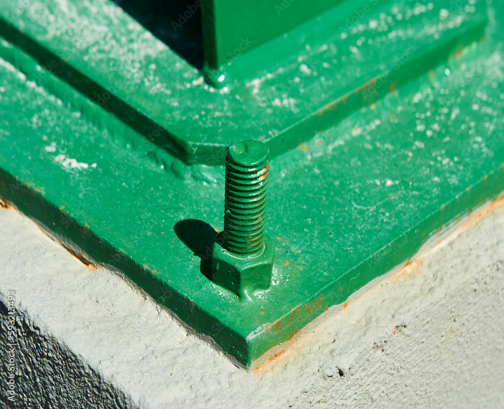 green painted bolt with nut bolted to a concrete pad to hold a beam ...
