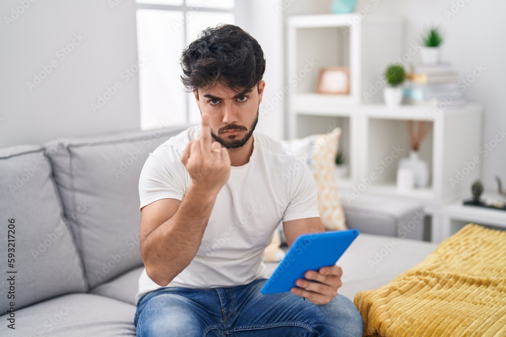 Hispanic man with beard using touchpad sitting on the sofa showing ...
