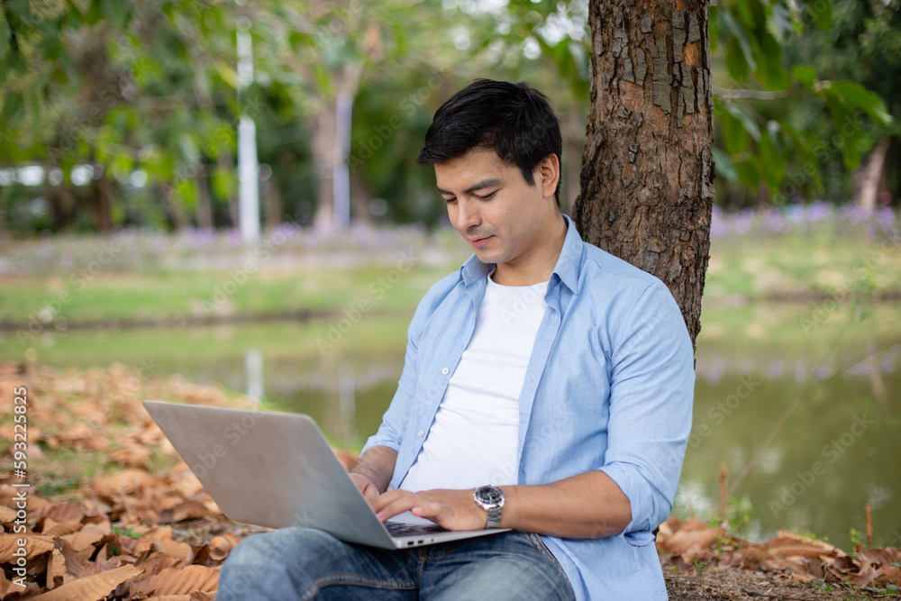 Handsome caucasian man working with laptop computer sitting under tree ...