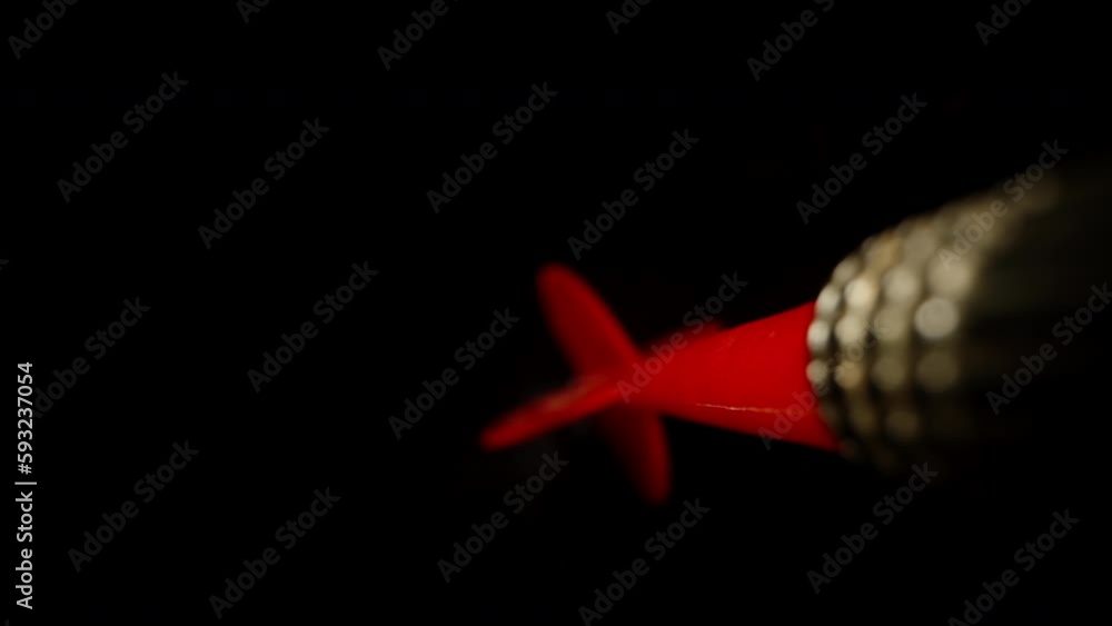 A red dart for playing darts rotates and flies on a black background to ...