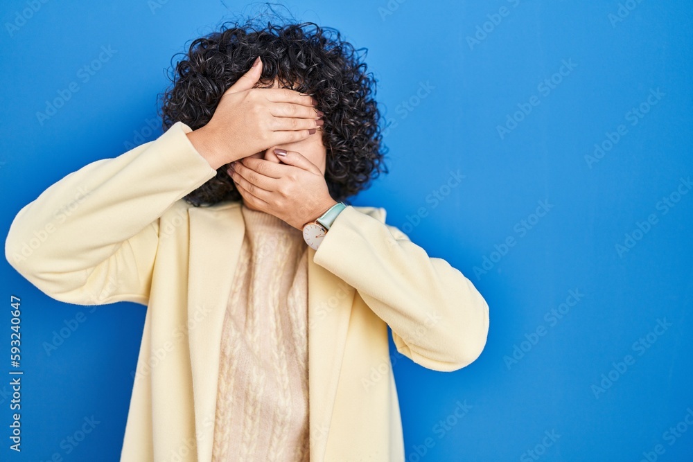 Young brunette woman with curly hair standing over blue background ...