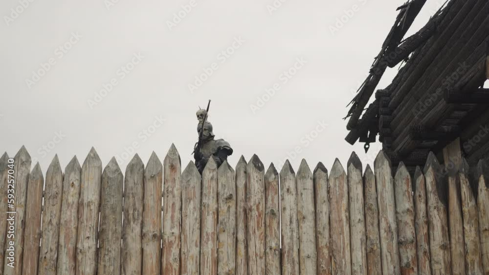 Evil knight with spear walks near burnt wooden house behind fence rain ...