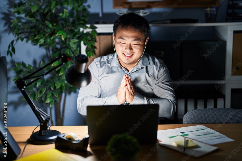 Young chinese man working using computer laptop at night praying with ...