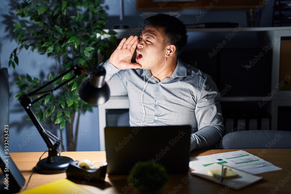 Young chinese man working using computer laptop at night shouting and ...