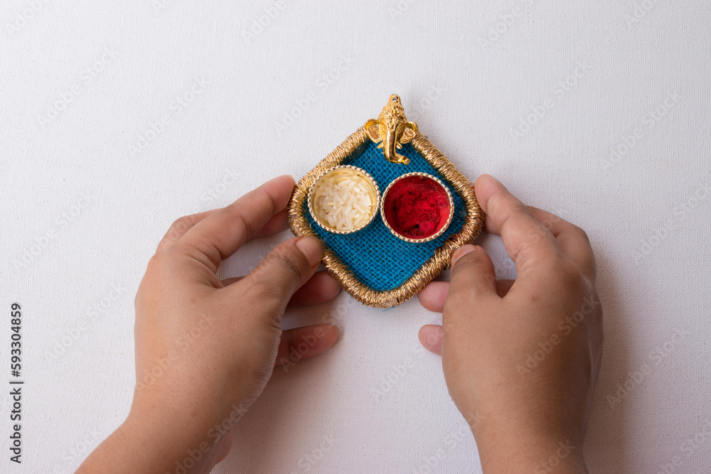 Hand holding beautiful small thali having God Ganesh face and red roli ...