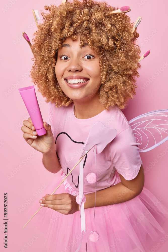 Vertical shot of cheerful curly haired female tooth fairy holds ...