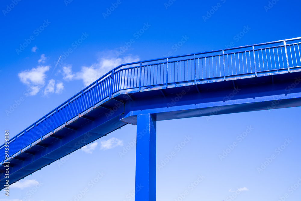 A modern pedestrian overpass across a highway. Blue bridge without ...