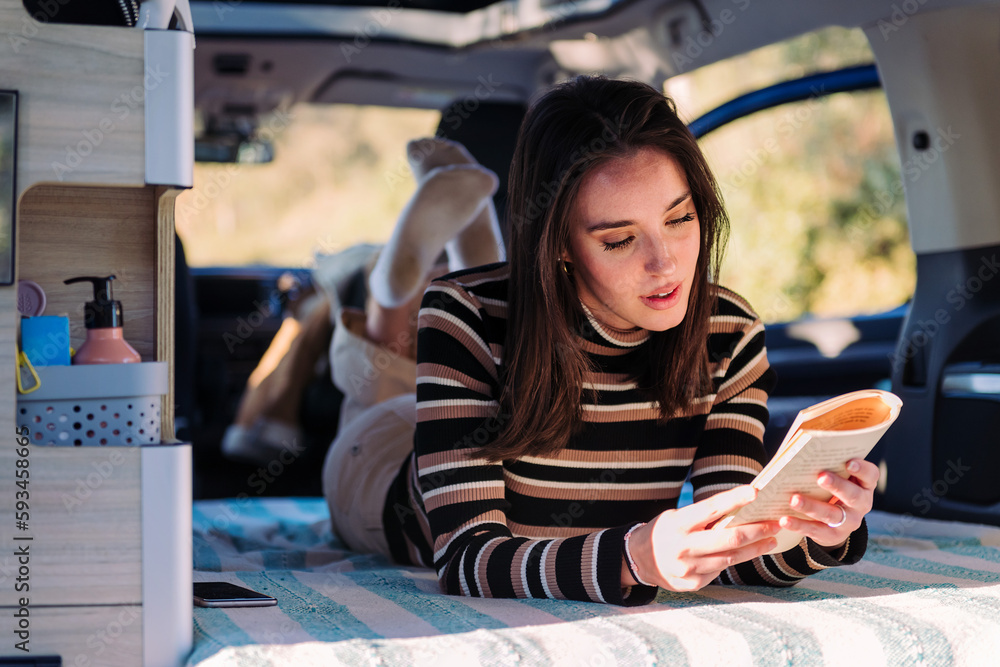 young caucasian woman relaxing in camper van reading a book, concept of ...