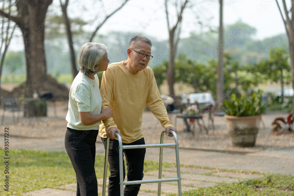 A wife helping her elderly husband patient use a walker to learn to ...