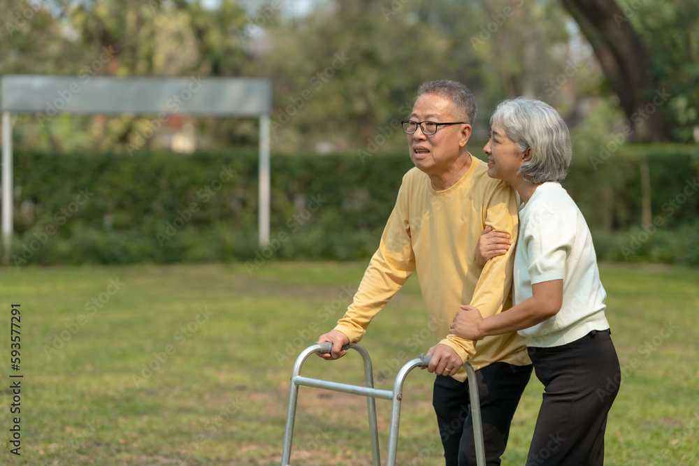 A wife helping her elderly husband patient use a walker to learn to ...