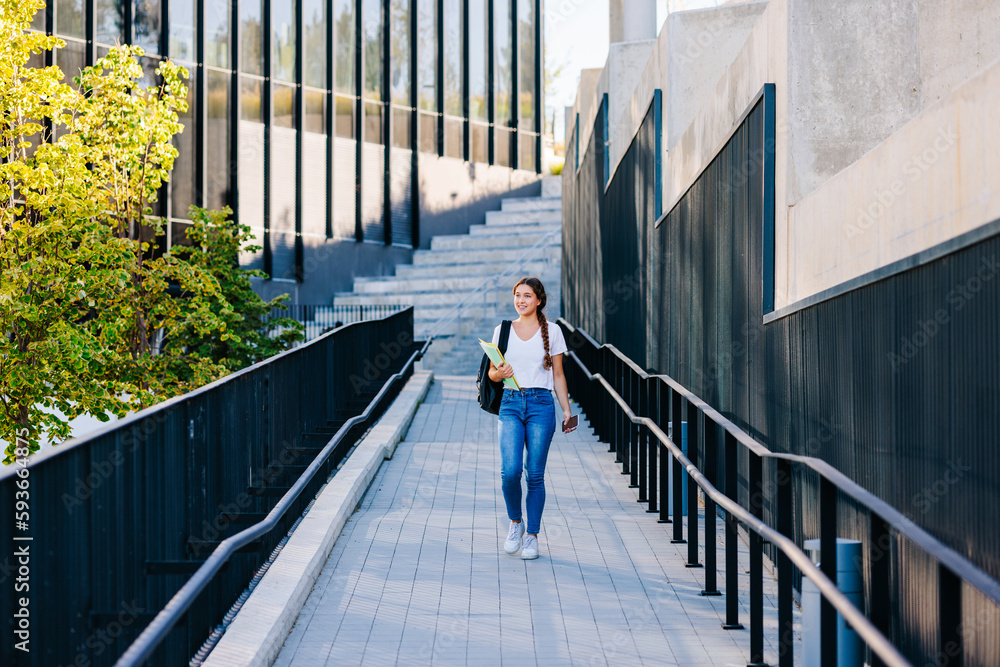 Smiling blonde college student walking by her new university campus ...