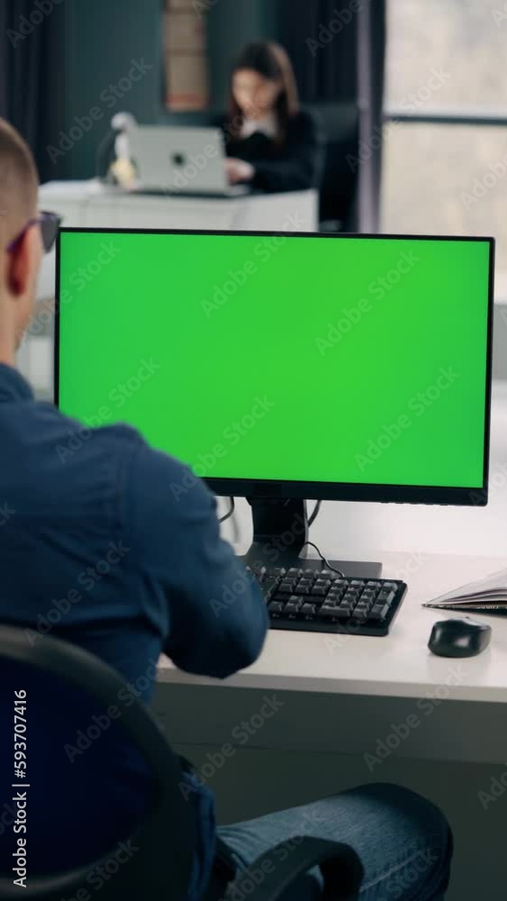 Young Man Working At Computer With Green Mock Up Screen in Office ...