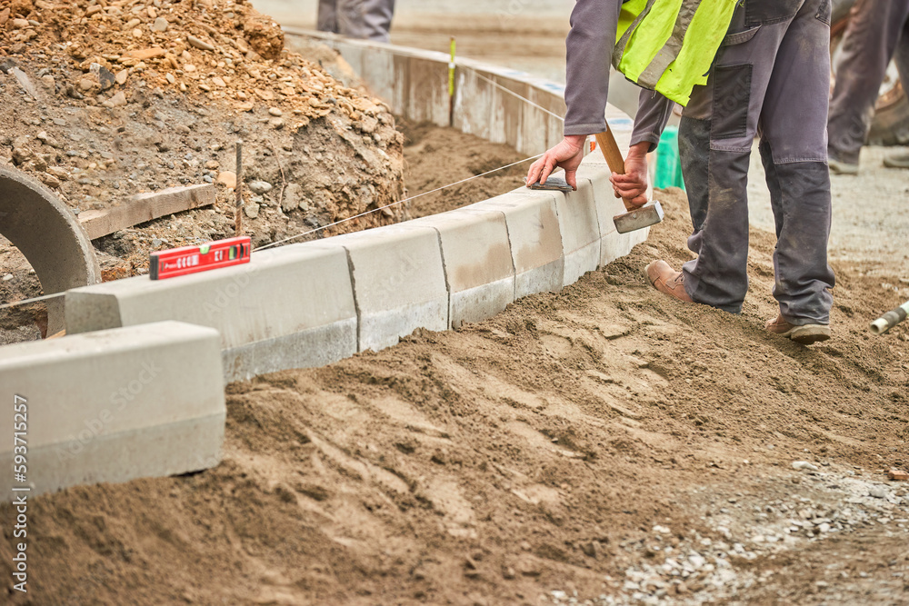 Progress of the road construction. Worker laying concrete curbs ...