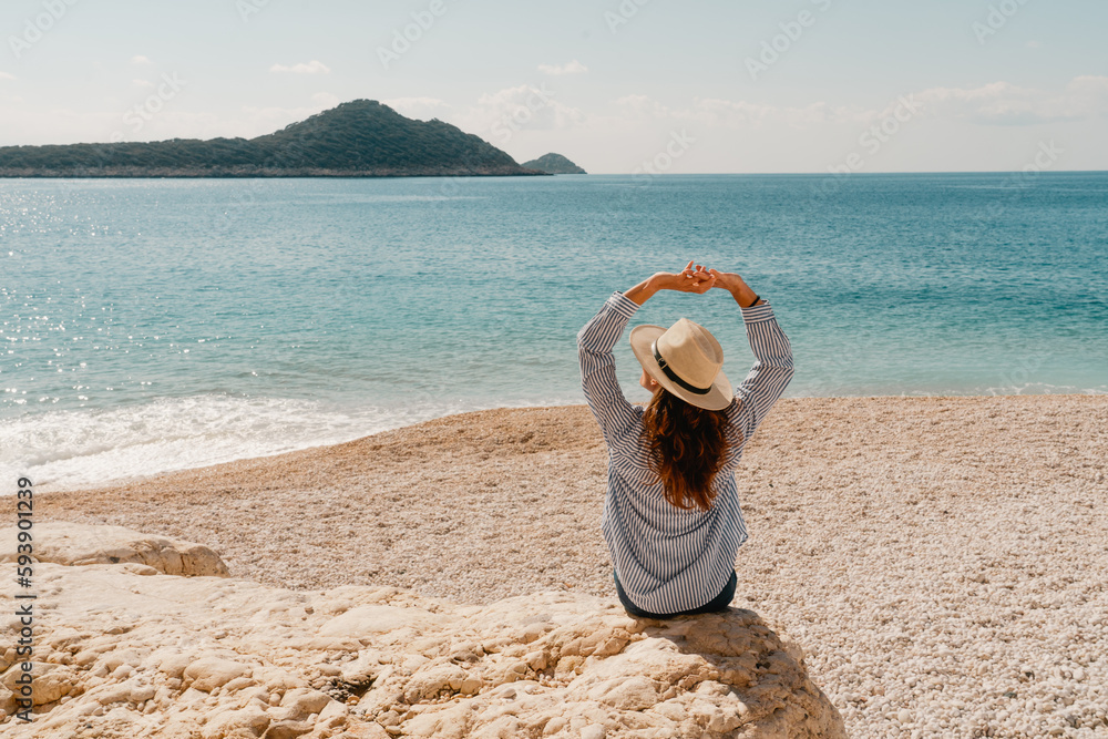 Woman wearing a hat sitting on the rock watching beautiful turquoise ...